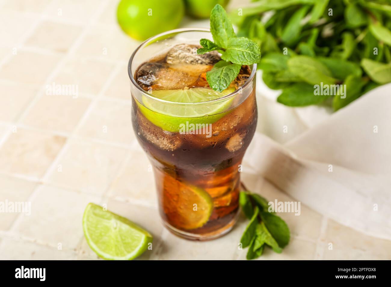 Glass of tasty Cuba Libre cocktail on light tile background Stock Photo ...