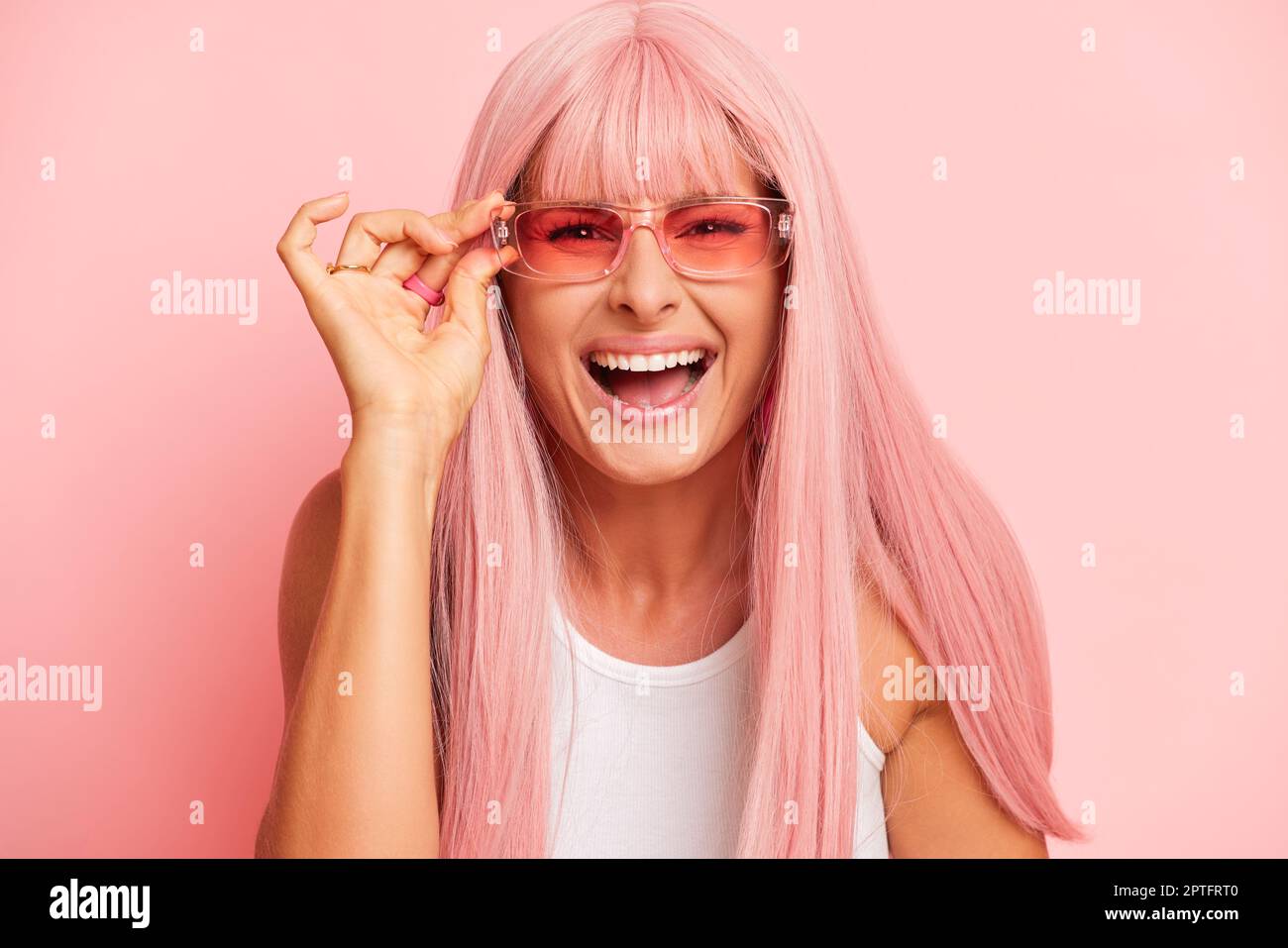 Lovely smiling young woman with pink wig posing on studio pink ...