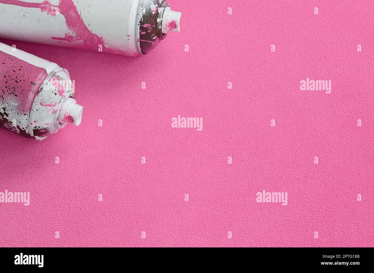 Some used pink aerosol spray cans with paint drips lies on a blanket of ...