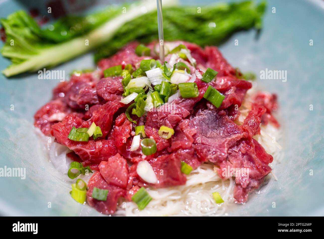 Boiling hot soup pour into noodle with slice of raw beef, famous ...