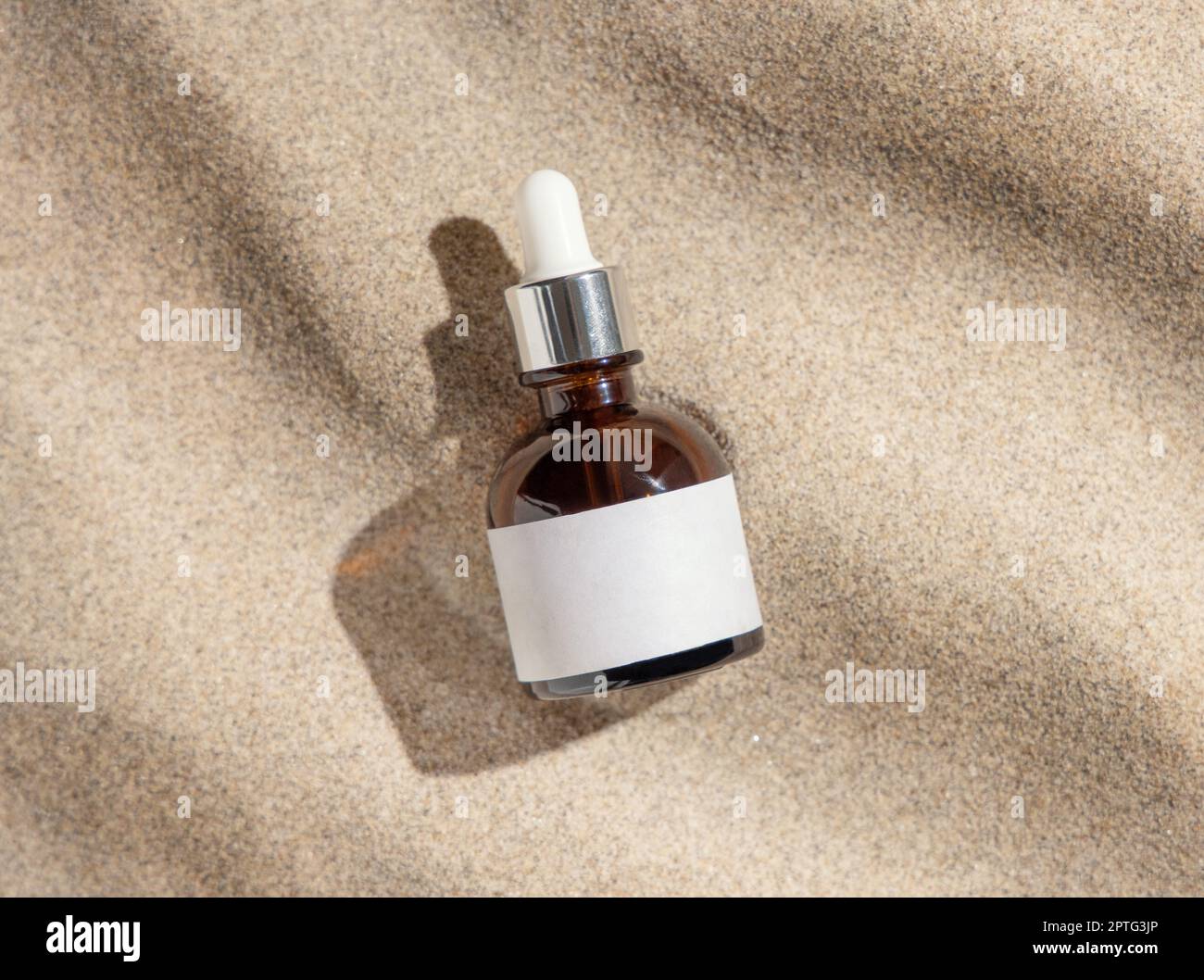 Dropper bottle with blank label on beige sand top view, hard light ...