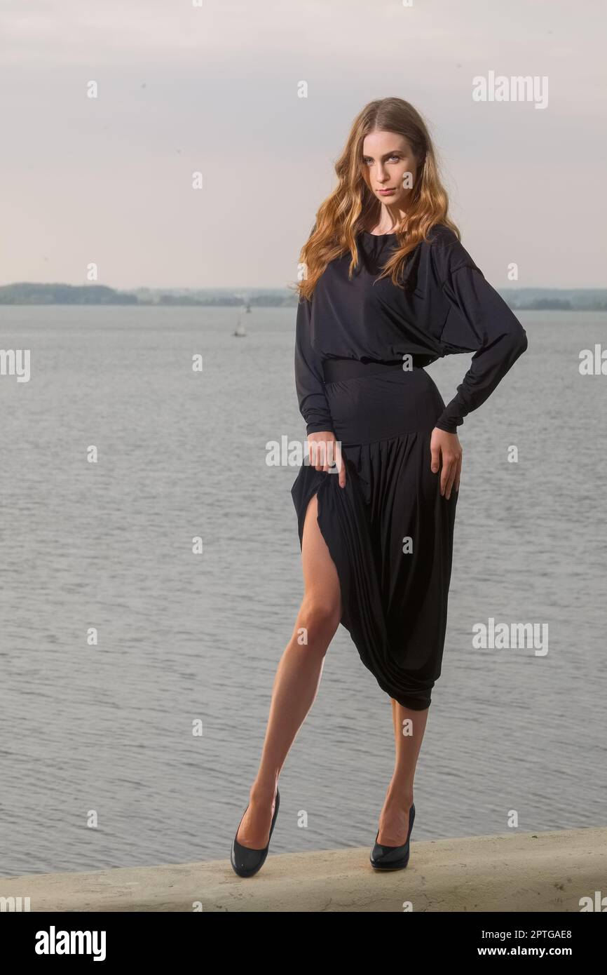 Attractive girl lifting long black dress and showing her slim legs on ...