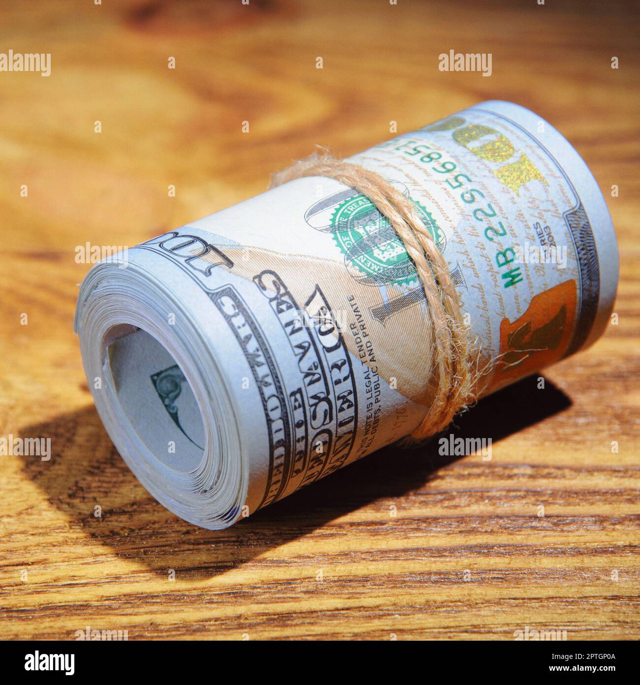 A roll of dollars on a wooden textured table in the dark illuminated by ...