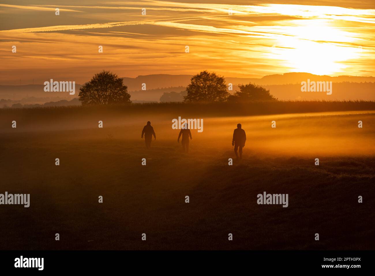 sunrise with three people walking through the mist Stock Photo - Alamy