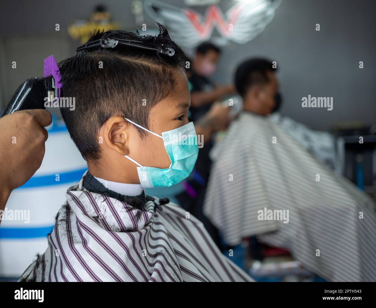 Teenage boy in a face protective mask is getting a haircut from a ...
