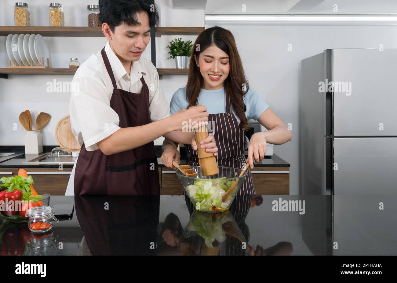 Young asian woman dressed in an apron mix the vegetables together with a wooden ladle. Tomato ...