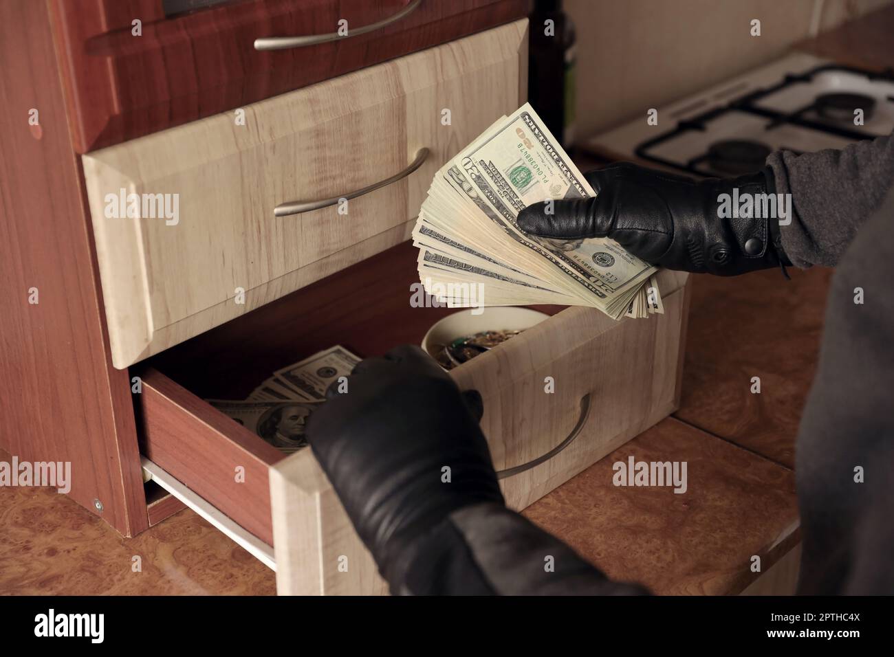 Robber in black outfit and gloves see in opened shelf in kitchen. The ...