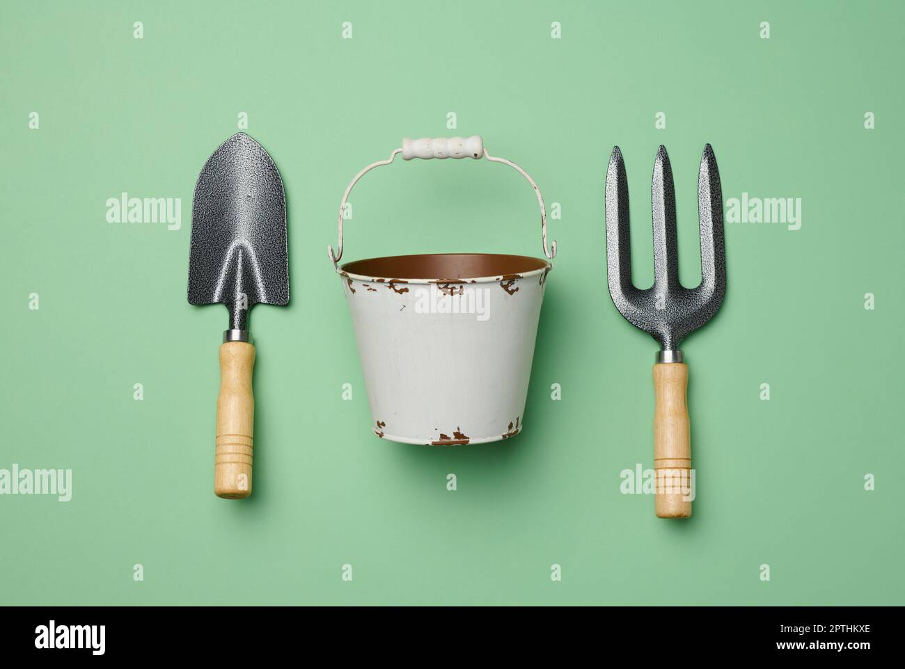 Miniature garden tools in a metal bucket on a green background, top ...