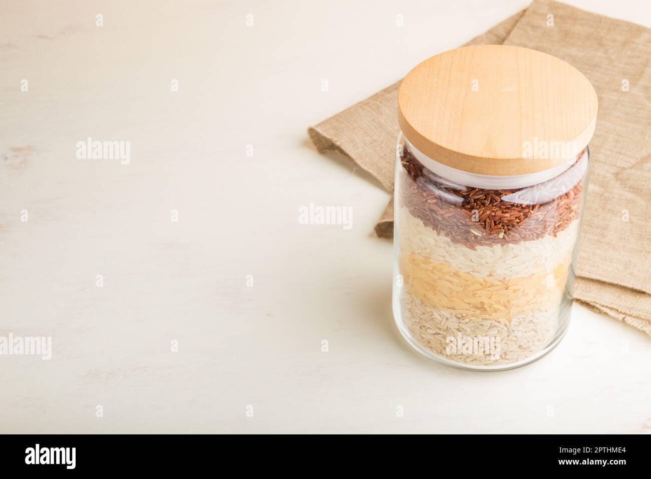 glass jar with different kinds of rice poured in layers on white ...