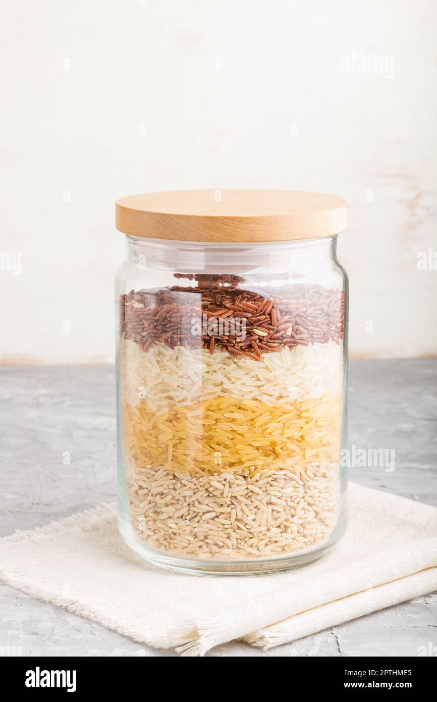 glass jar with different kinds of rice poured in layers on a gray and ...