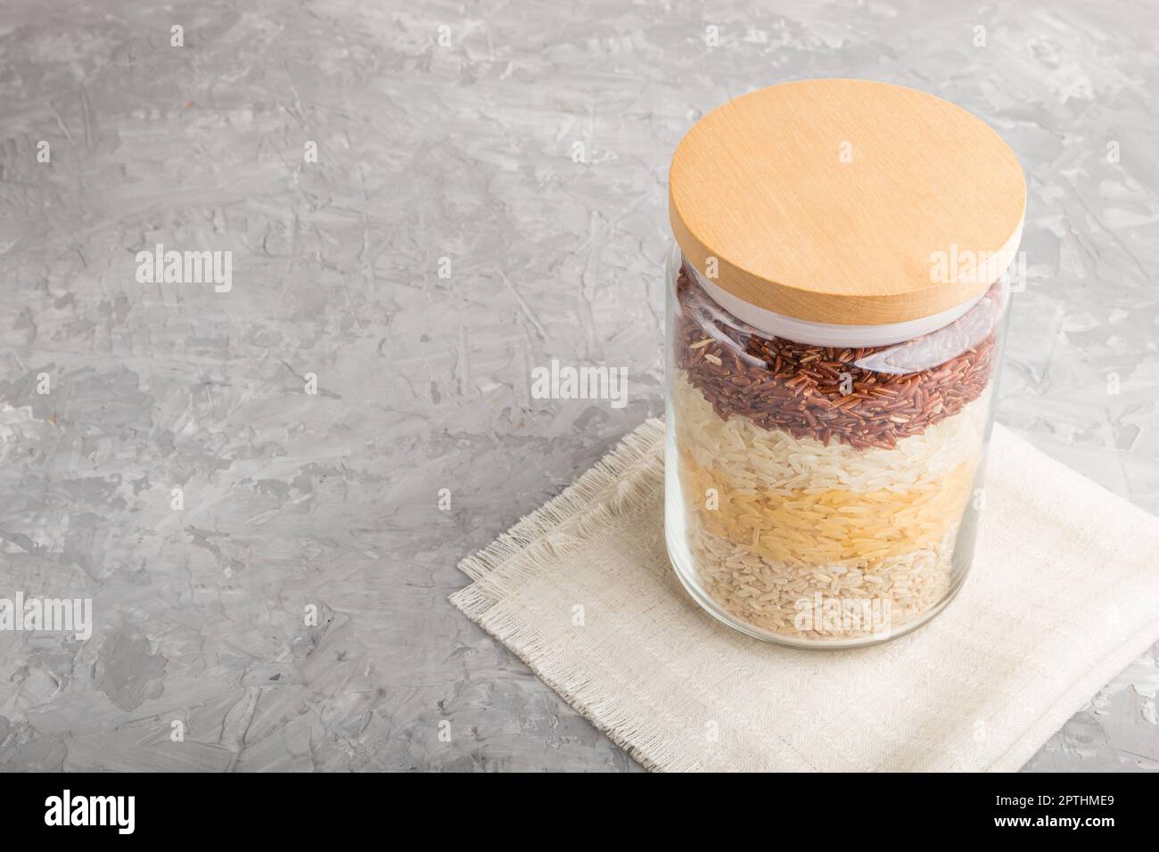 glass jar with different kinds of rice poured in layers on a gray ...