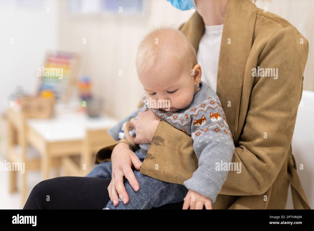 Mother holding infant baby boy in her lap, sitting and waiting in front ...