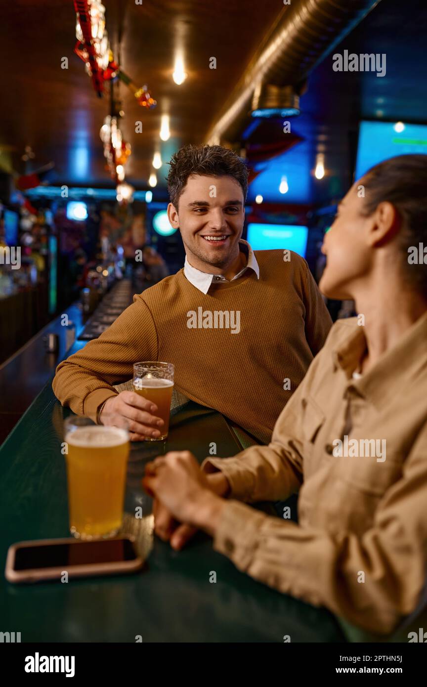 Young man and woman talking while enjoying drinks together at sport pub ...