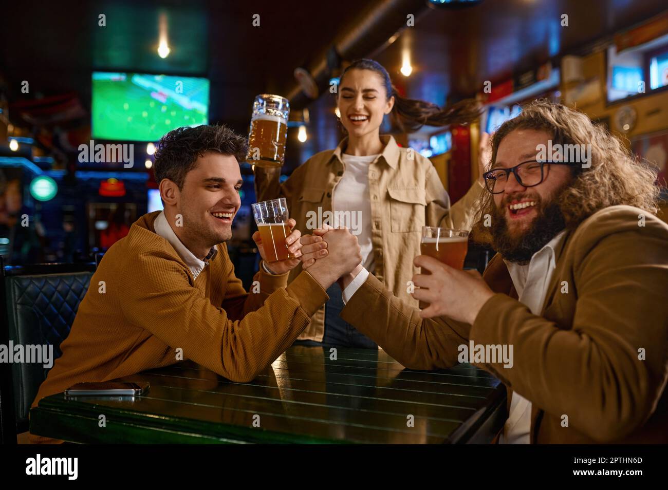Happy friends having fun arm wrestling during rest at sport bar. Funny ...