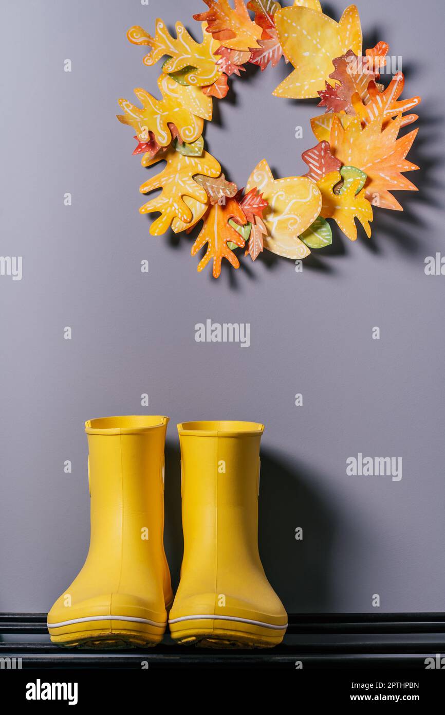 Homemade autumn yellow-red paper wreath and yellow rubber boots on gray ...