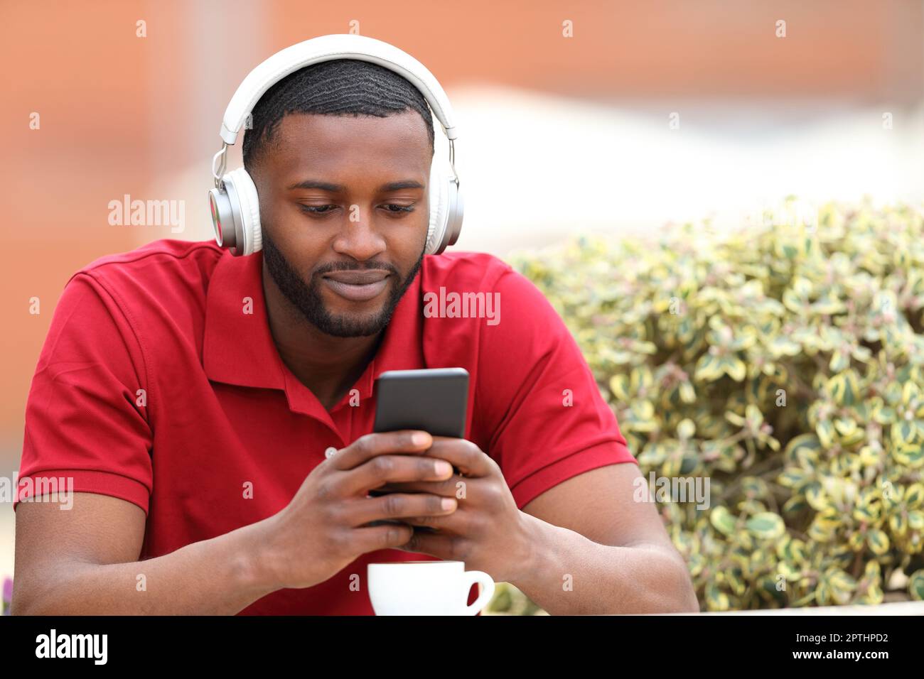 Black man wearing headphones listening to music checking smart phone in ...