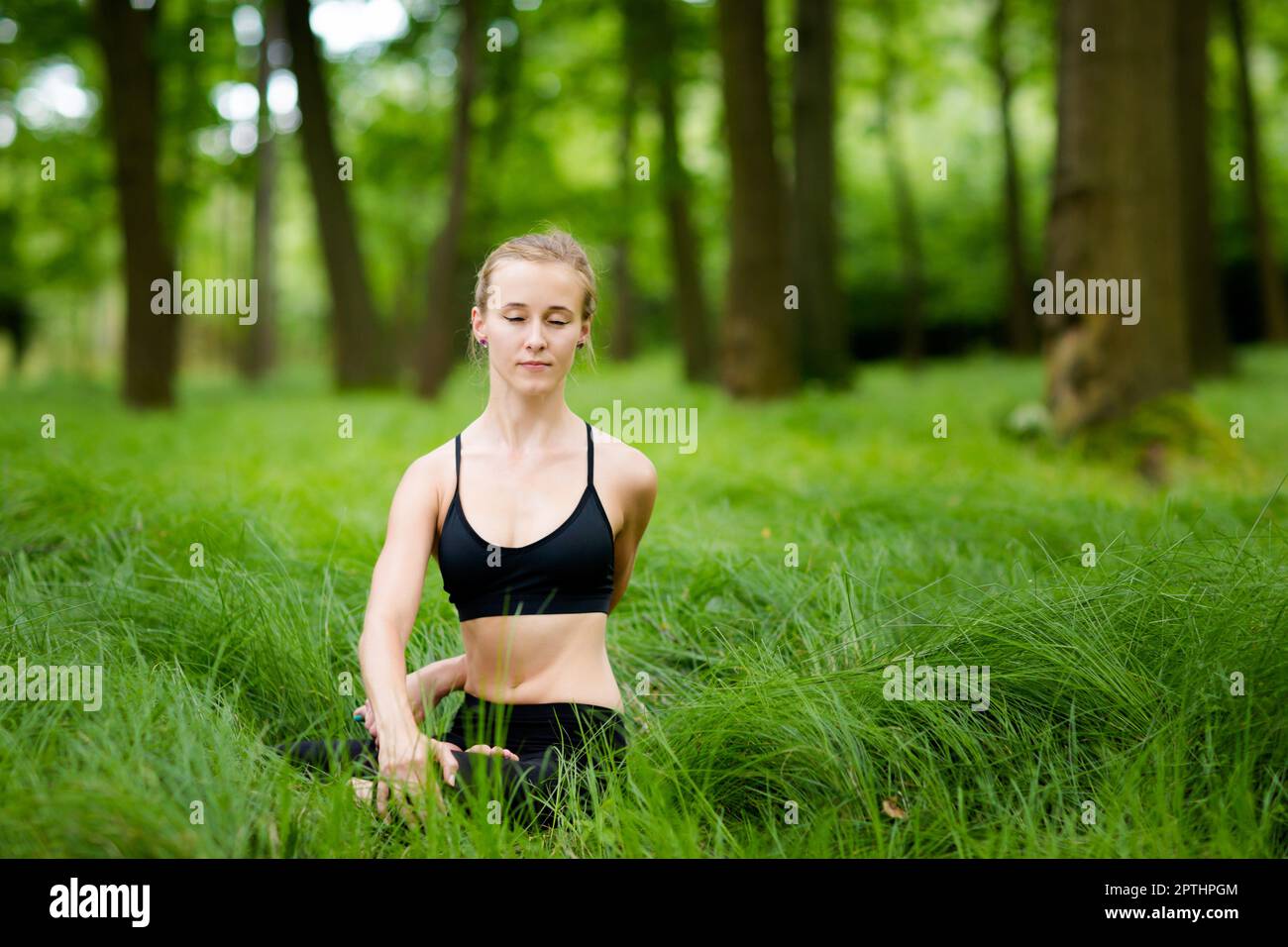 Nature yoga session in beautiful green polish woods, between trees. Meditation -twisted lotus ...