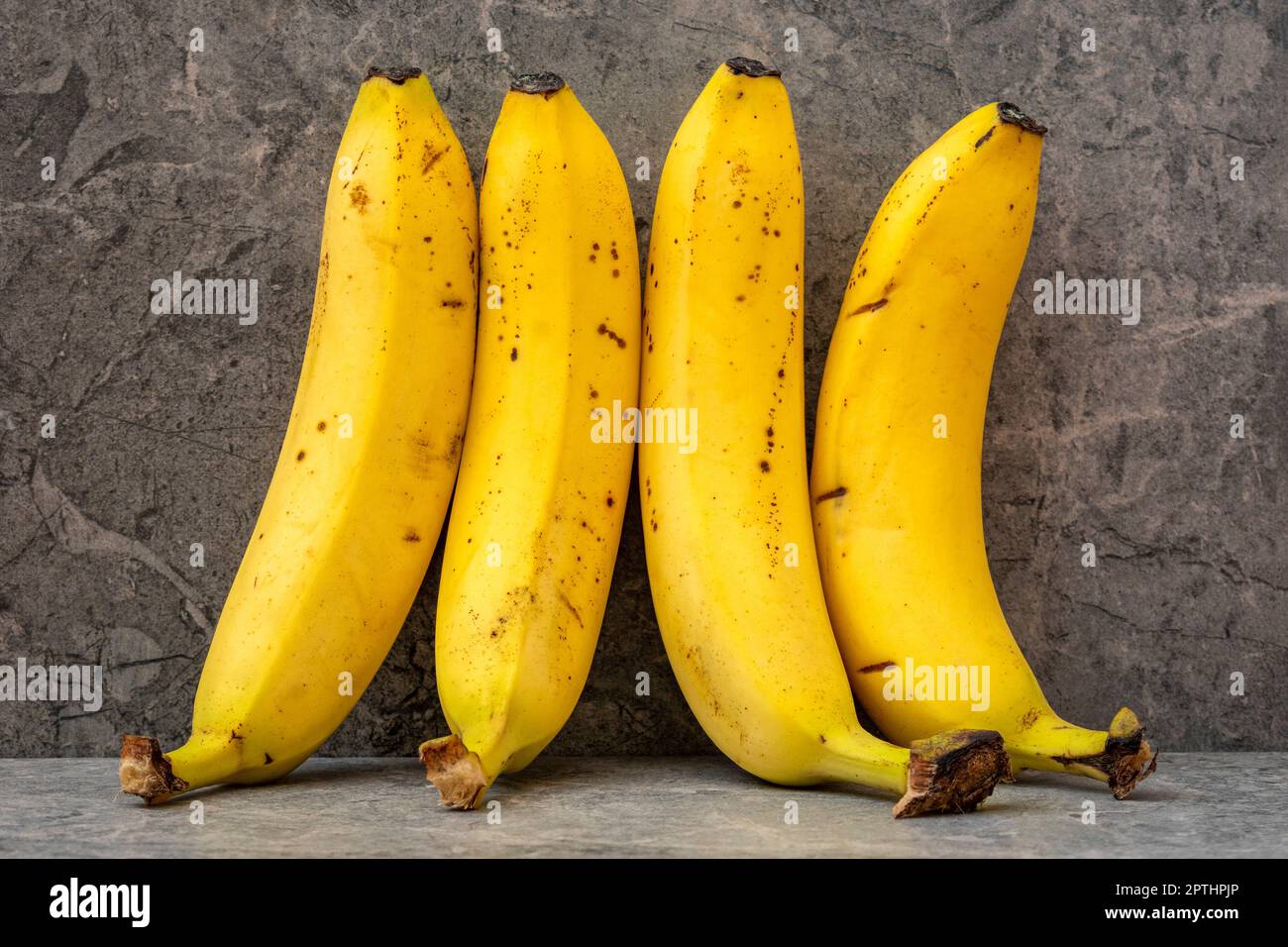 Four yellow bananas leaning on a grey stone background. Healthy food ...