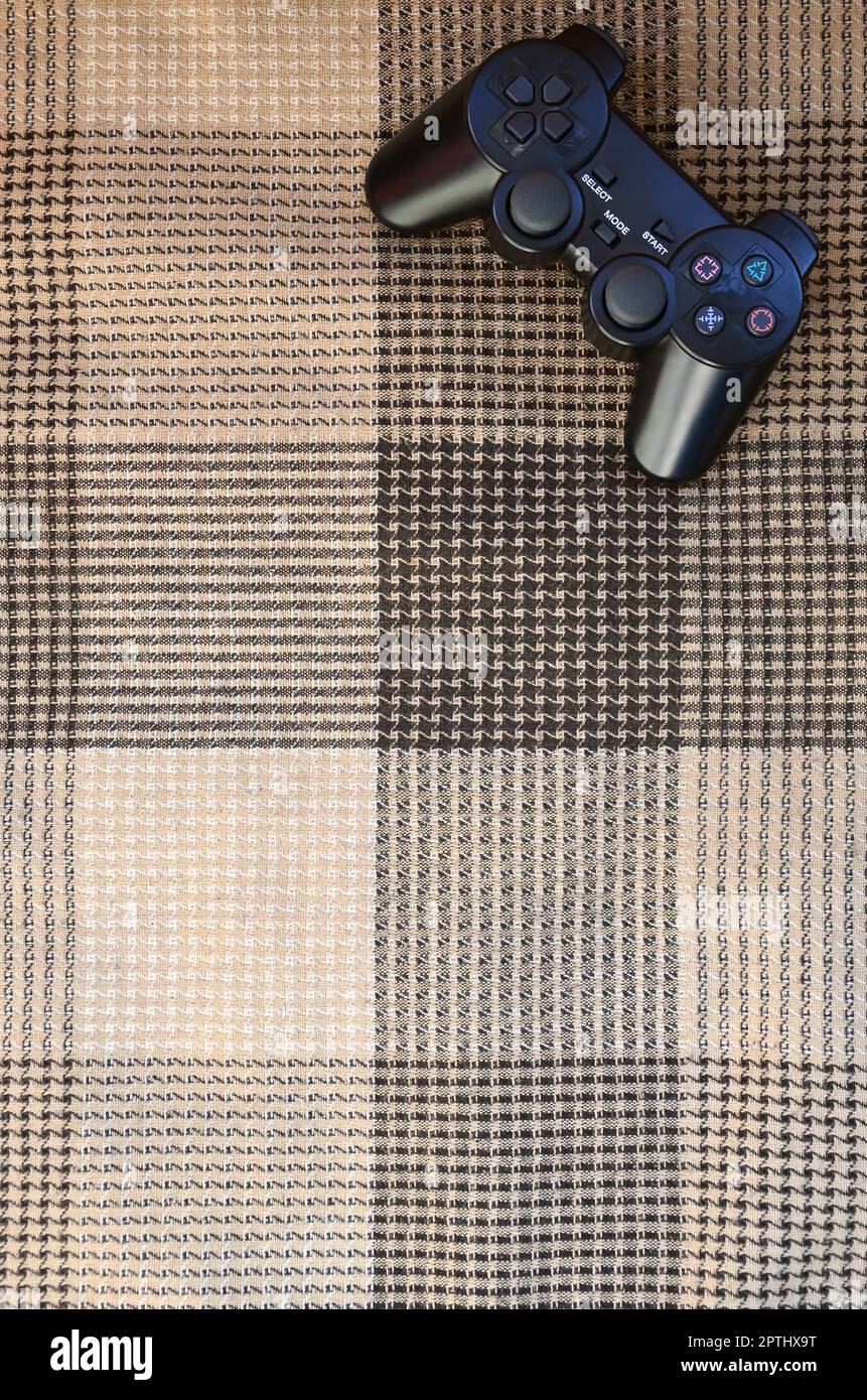 Modern black video game controller lies on a checkered beige and black ...