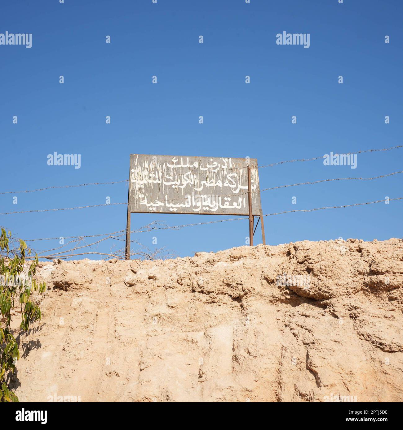 Board with arabic letters with blue sky and wired fence in the ...
