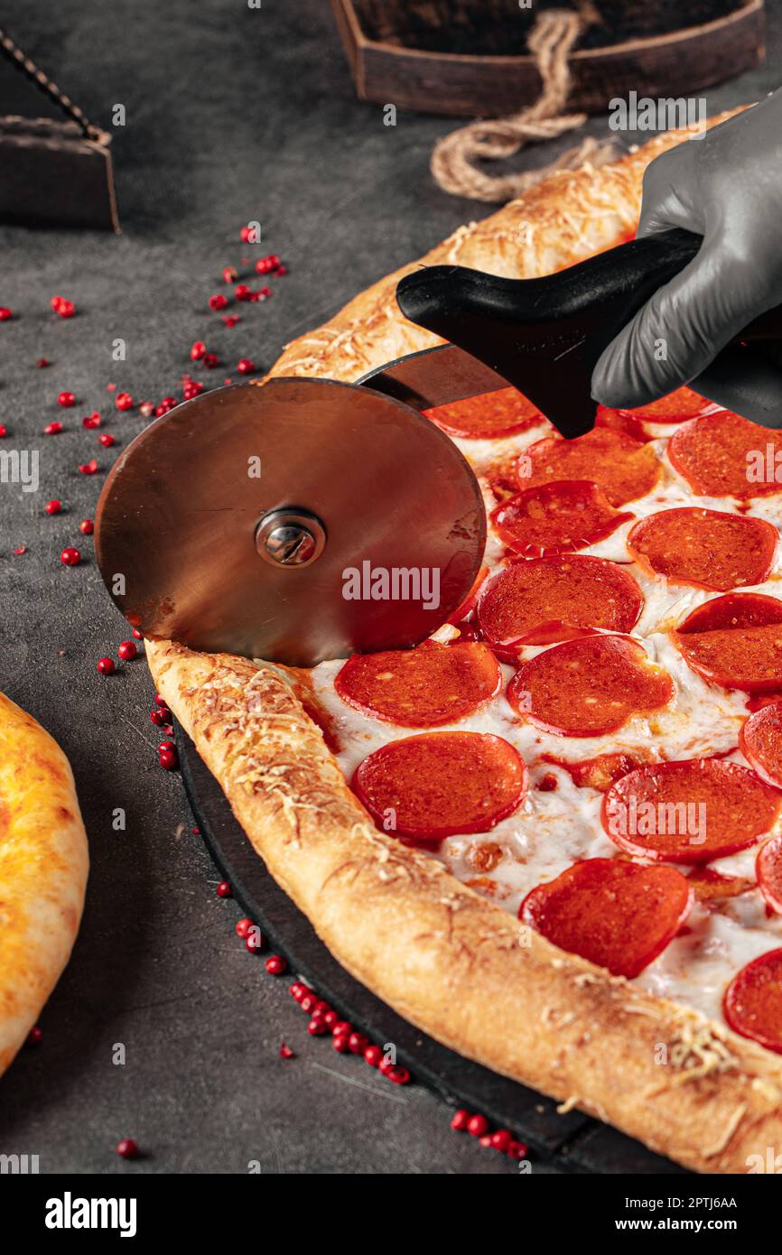 Cutting giant pepperoni pizza with special knife Stock Photo - Alamy