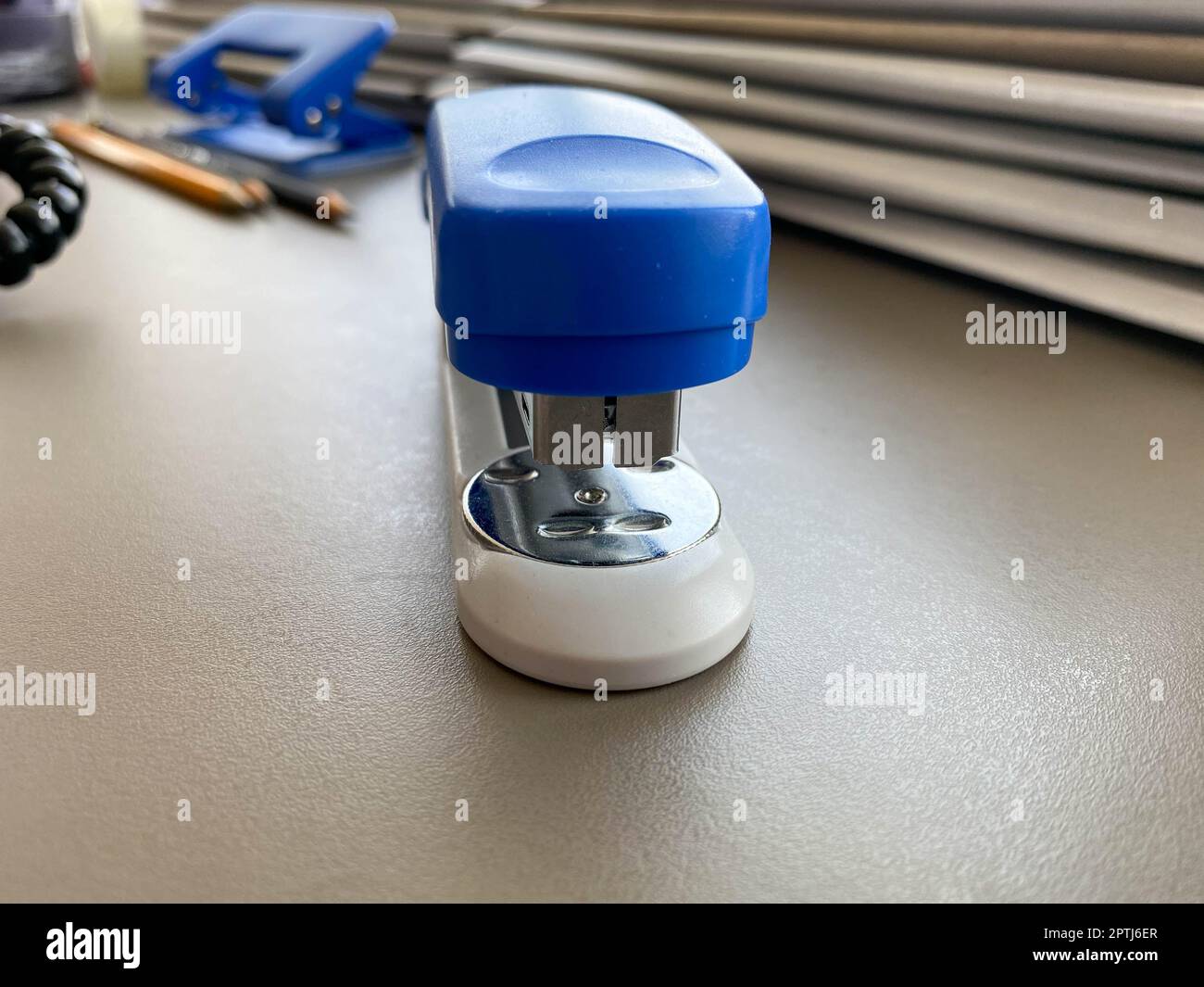 A large blue stapler for stapling paper lies next to the folders of ...