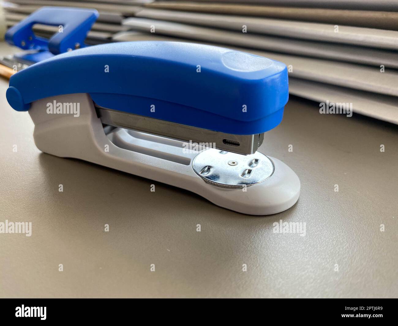 A large blue stapler for stapling paper lies next to the folders of ...
