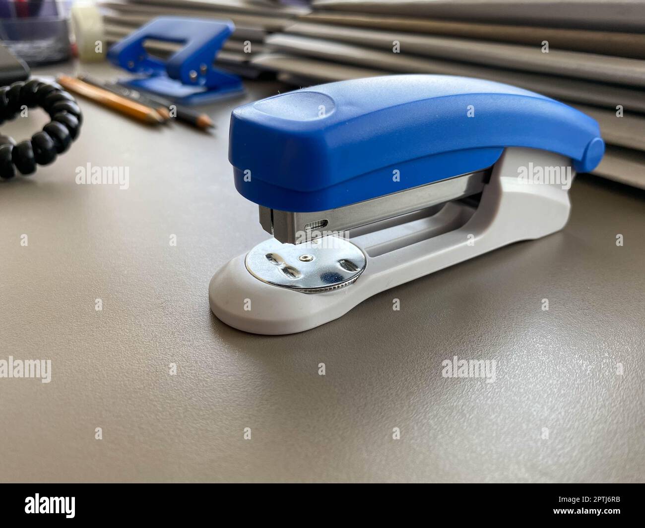 A large blue stapler for stapling paper lies next to the folders of ...