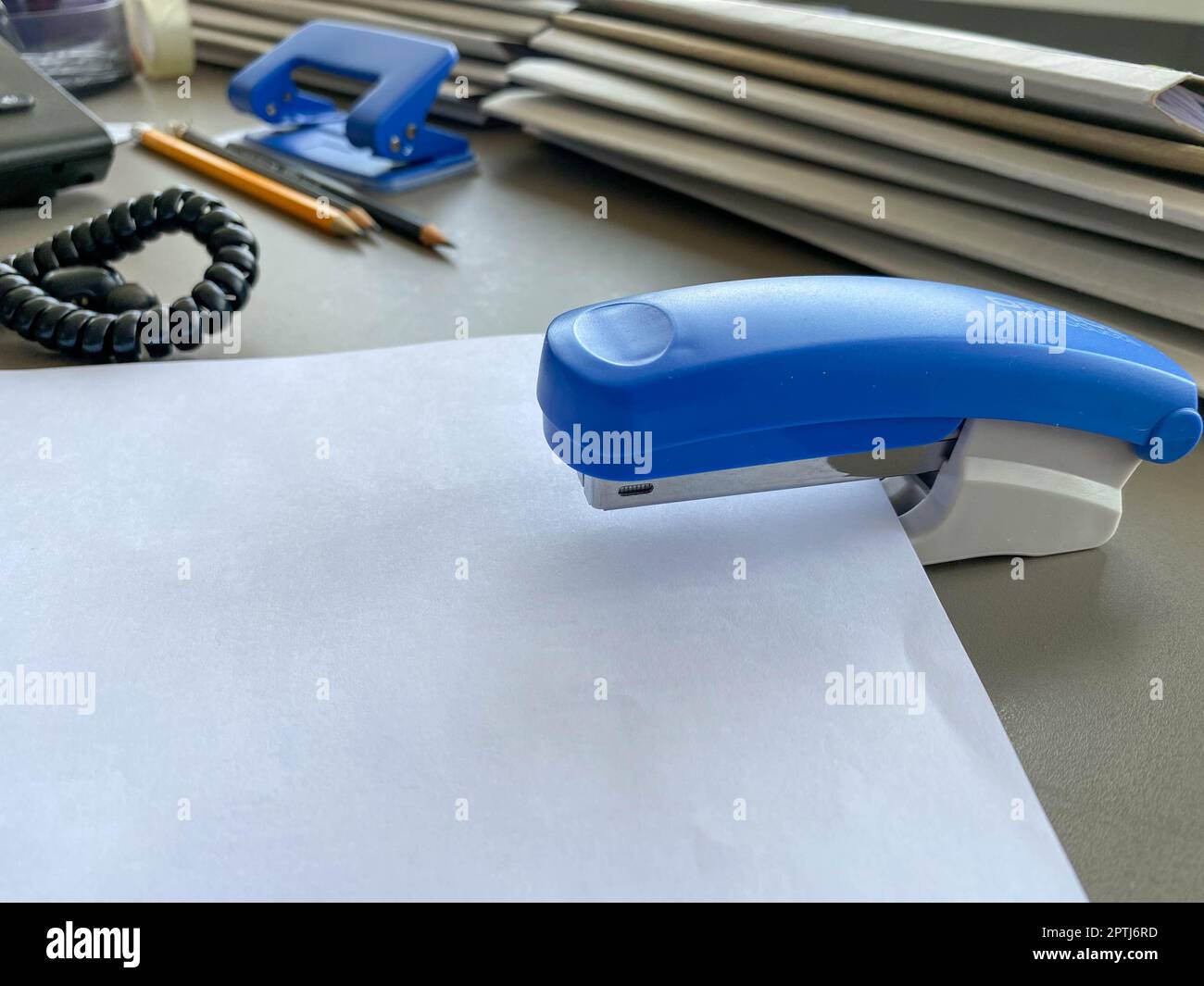 A large blue stapler for stapling paper lies next to the folders of ...