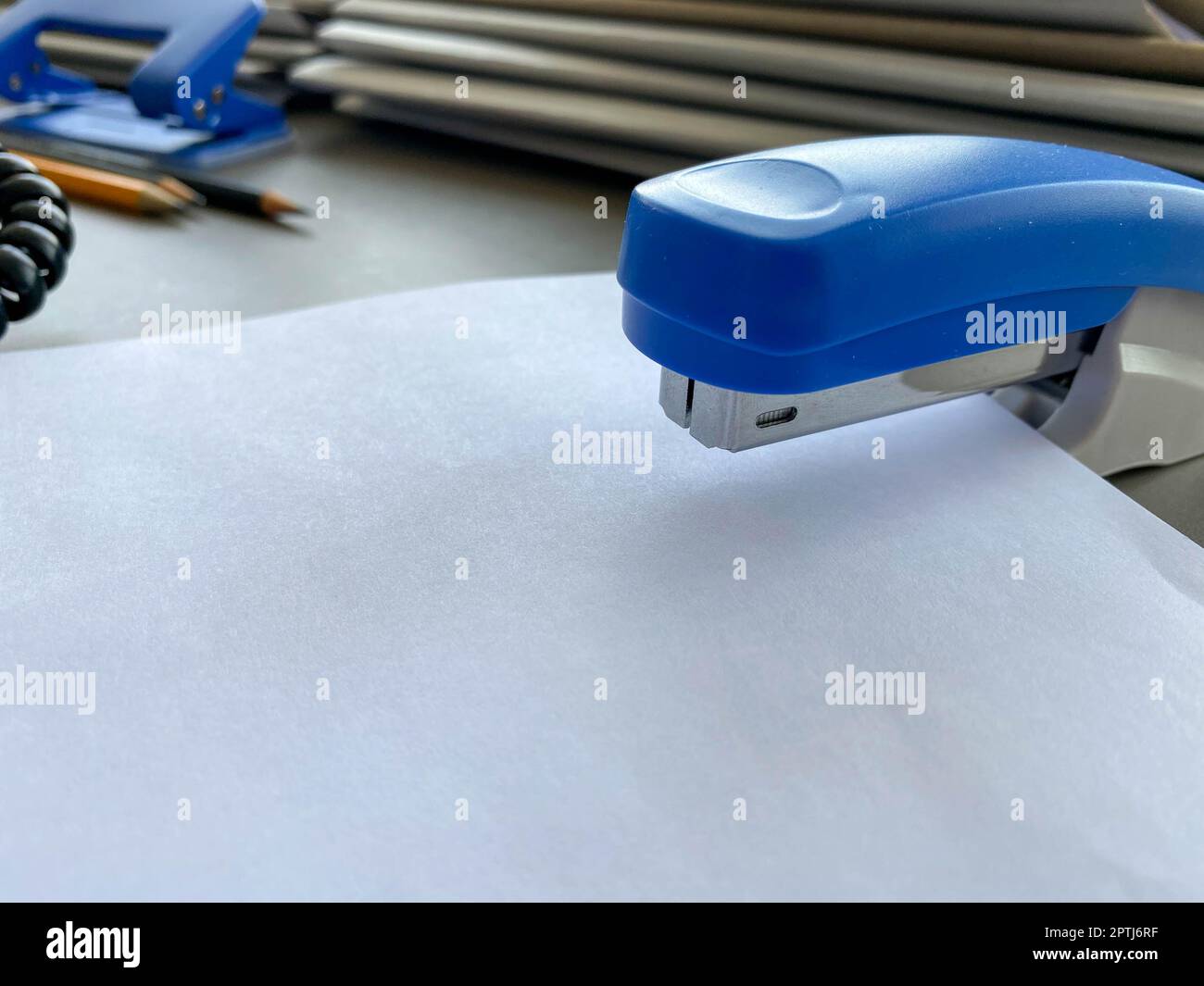A large blue stapler for stapling paper lies next to the folders of ...