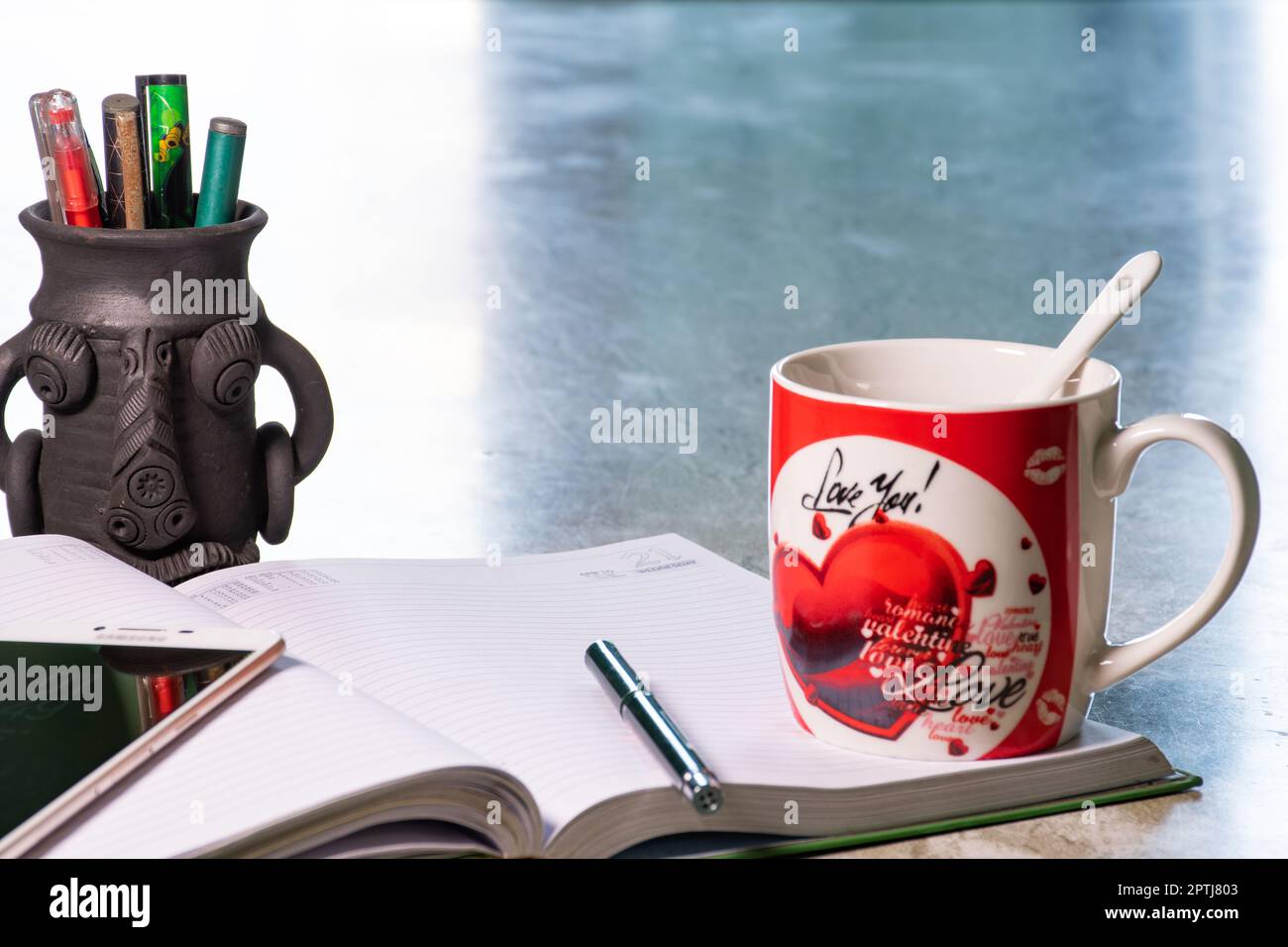 A red coffee mug with a glass spoon and a diary, a debit card, a cell ...