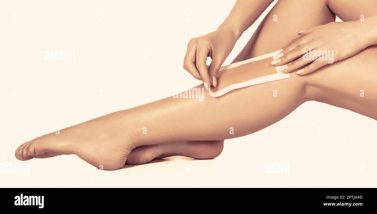 Waxing woman leg with wax strip at beauty spa. Close-up waxing woman leg in spa. Well-groomed ...