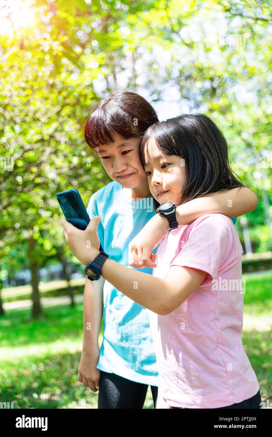 Two sisters hugging while using mobile phone in the park. Happy family ...
