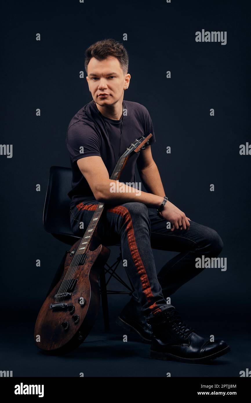 Low key portrait of musician sitting on chair with guitar Stock Photo ...