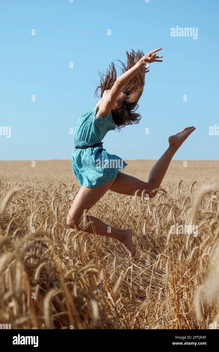 Carefree girl in a blue sundress stands under the sun in a wheat field ...