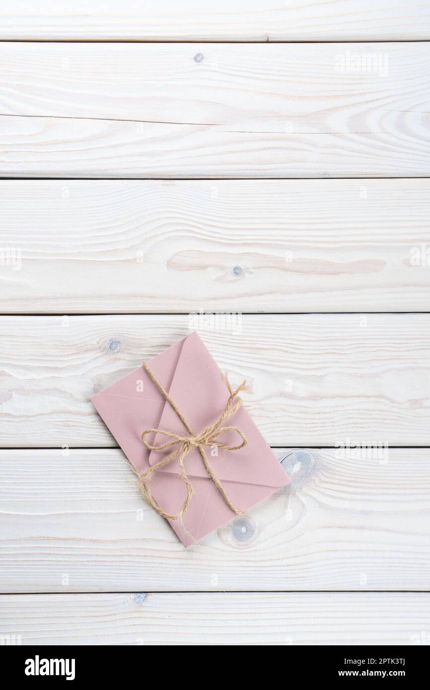 Pink envelope tied with rough jute rope on white wooden background ...