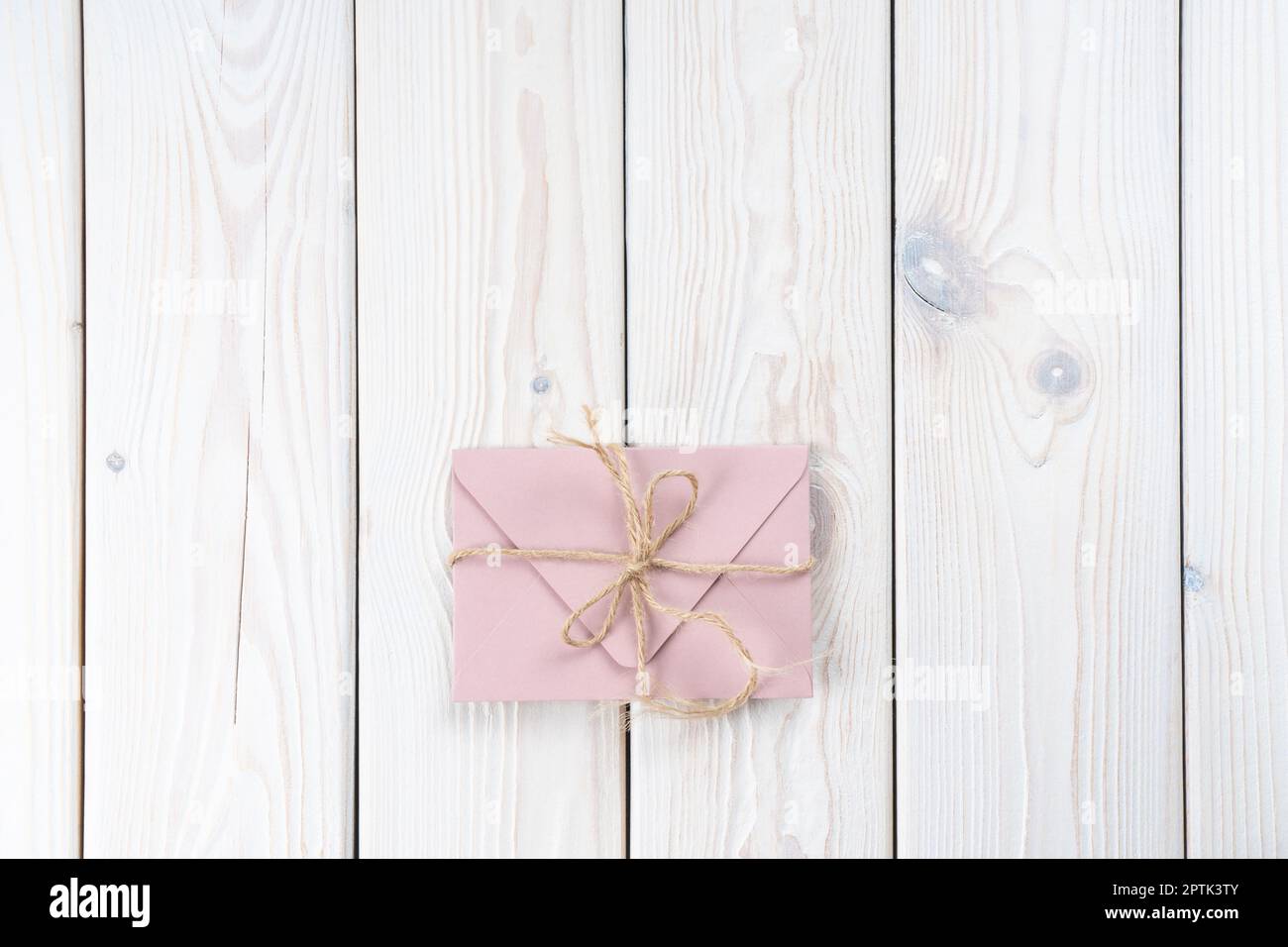 Pink envelope tied with rough jute rope on white wooden background ...