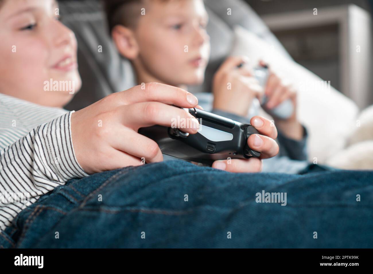 Side view of two teenage boys lying on sofa at home, holding gaming ...