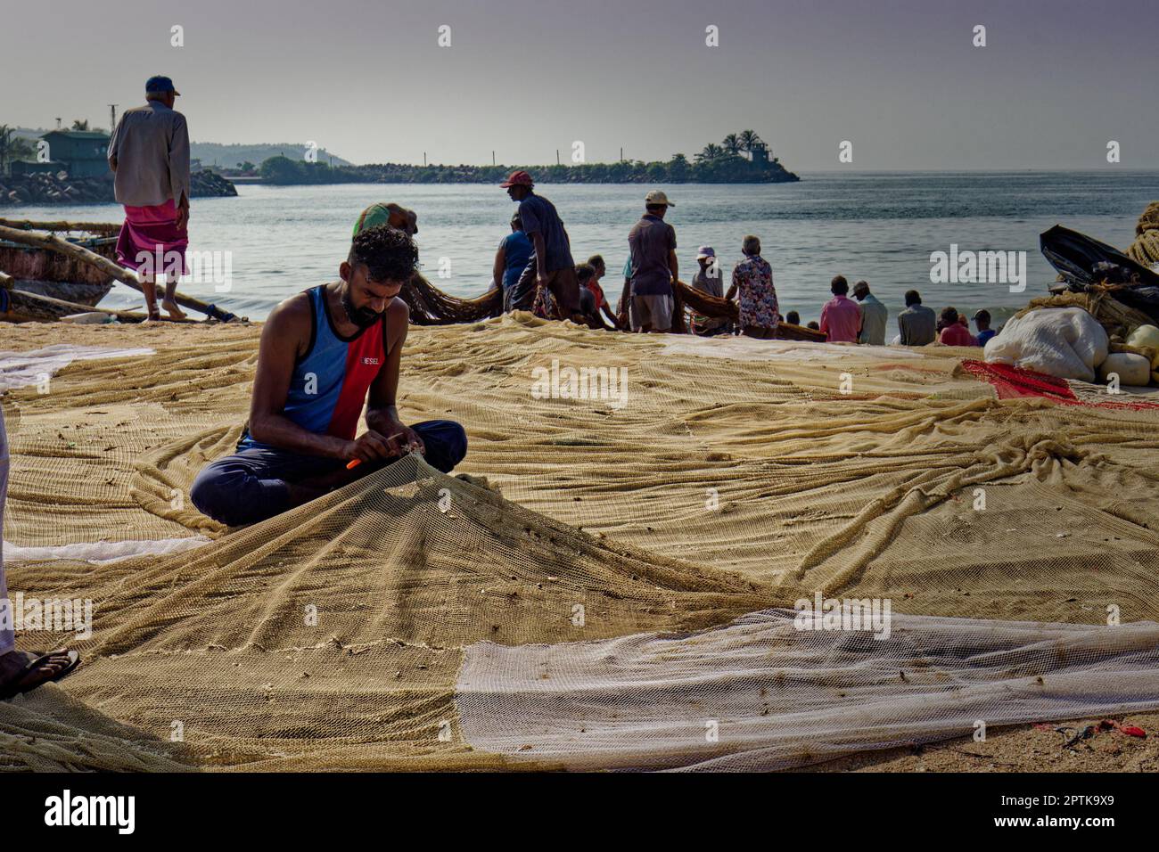 Fisherman weaving torn net in traditional way with fishing village ...