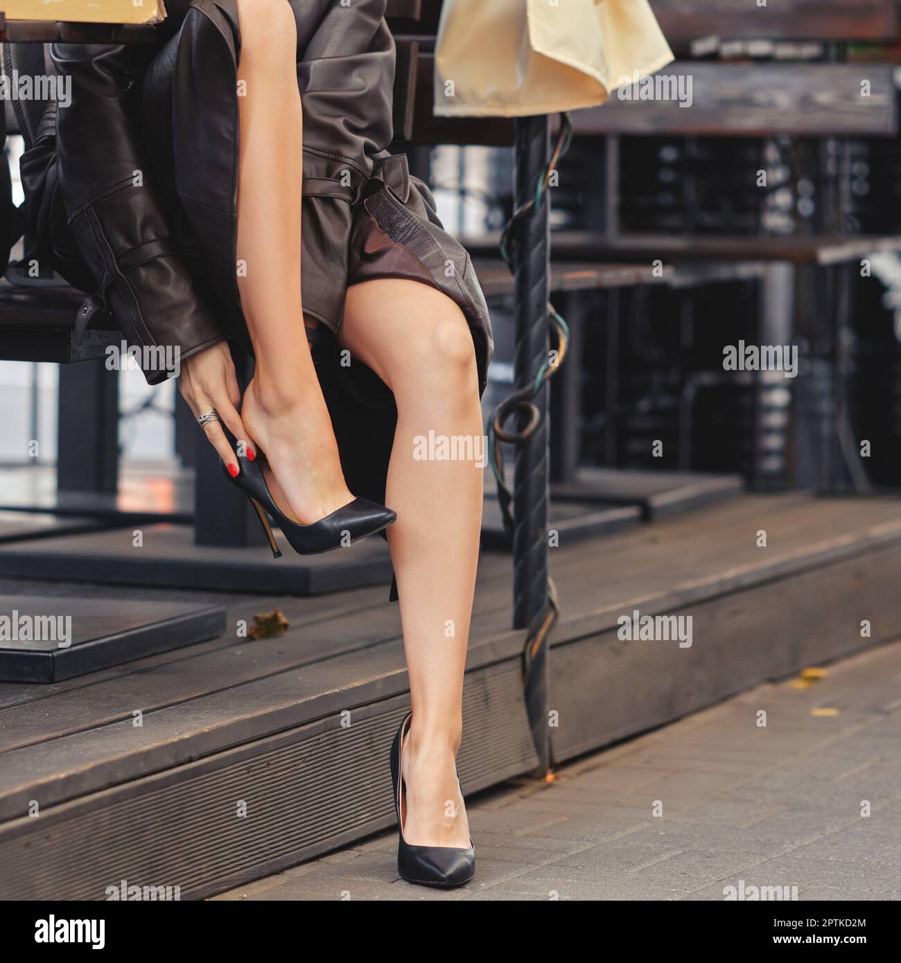 Unrecognizable woman in long coat sitting on bench and taking off shoe ...