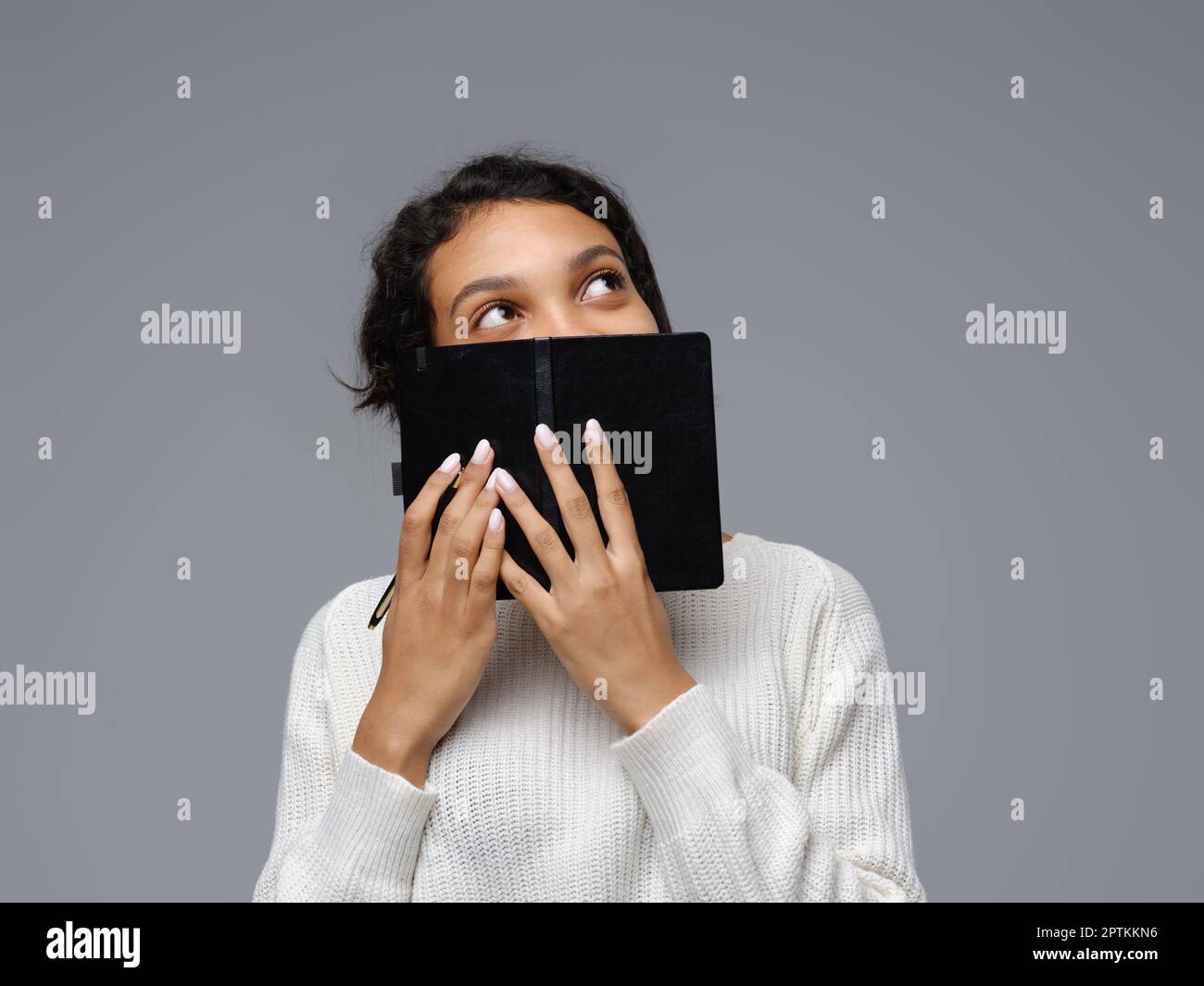Tricky young affican woman hide her face with notebook and looks up ...