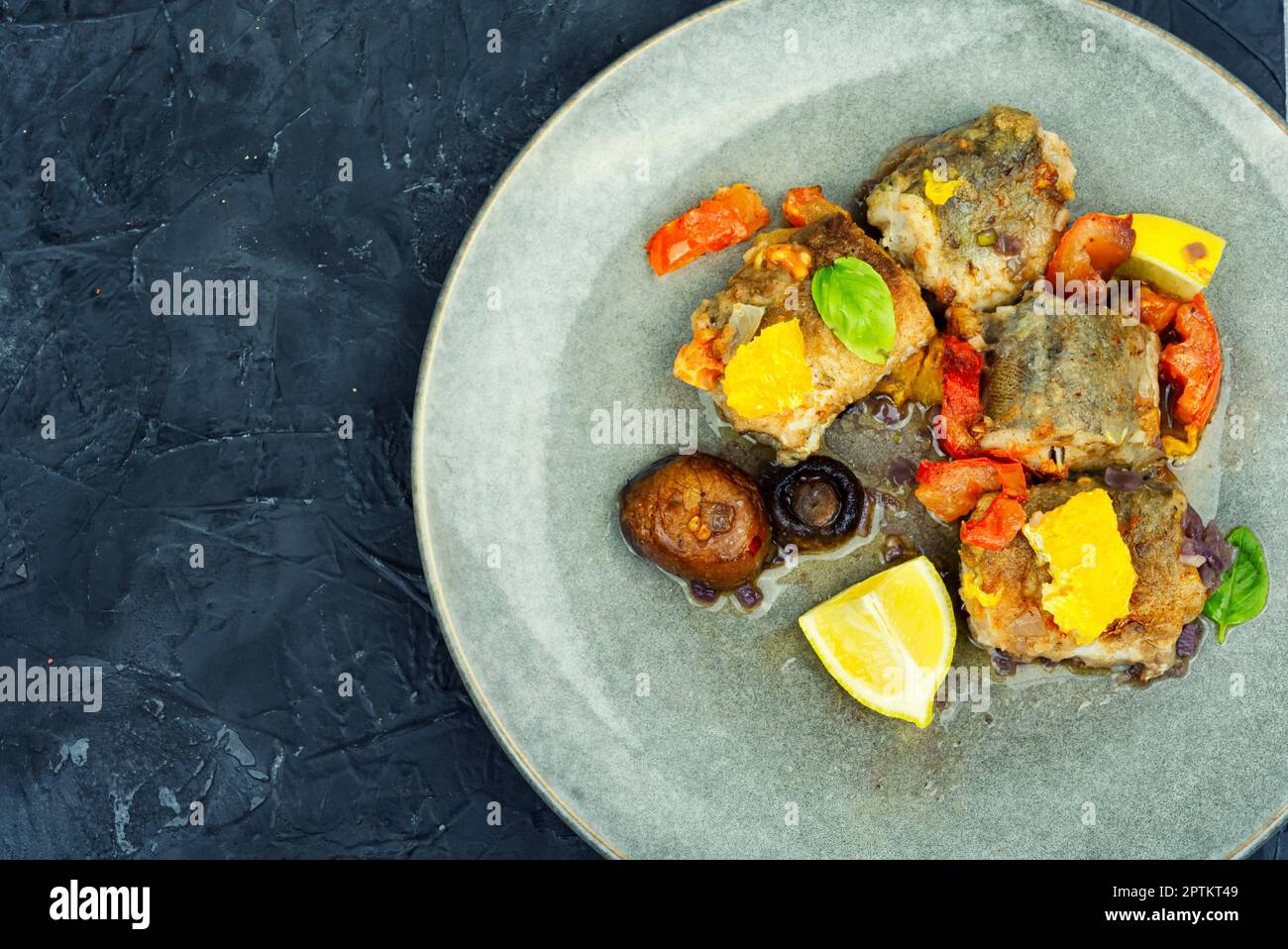 Baked hake fish on the plate. White fish with orange and mushrooms ...