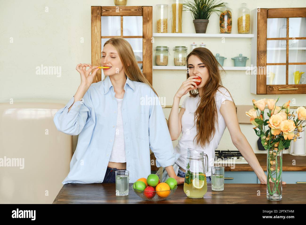 Two beautiful young women eat fruits in the kitchen Stock Photo - Alamy