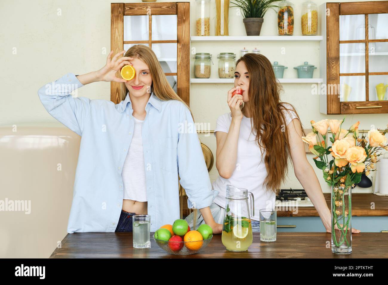 Two beautiful young women eat fruits in the kitchen Stock Photo - Alamy