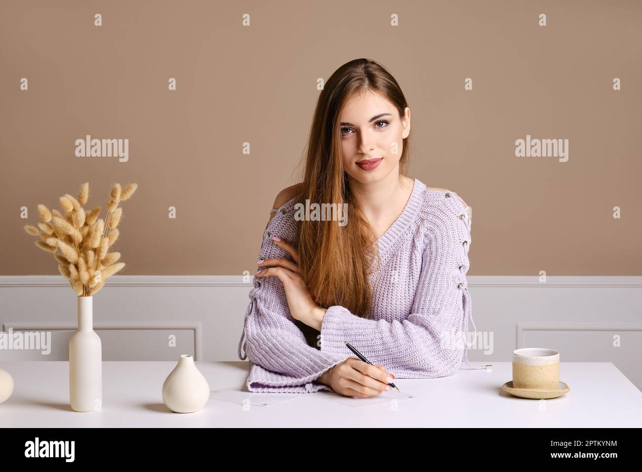 Kind young woman sits behind the table and signs greeting postcard ...