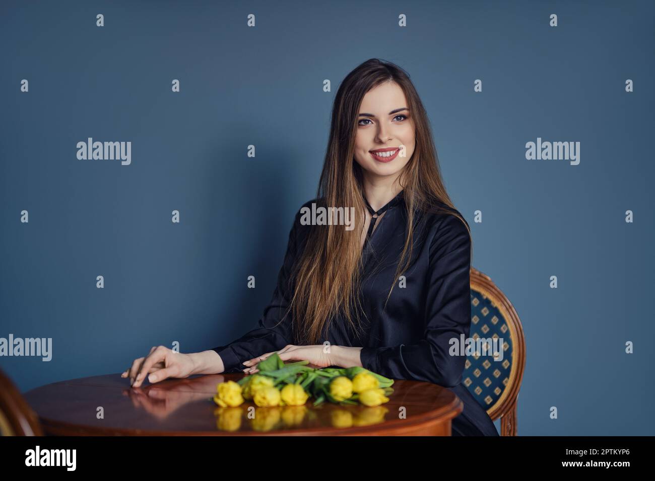Beautiful young woman sits behind the table with tulips Stock Photo - Alamy