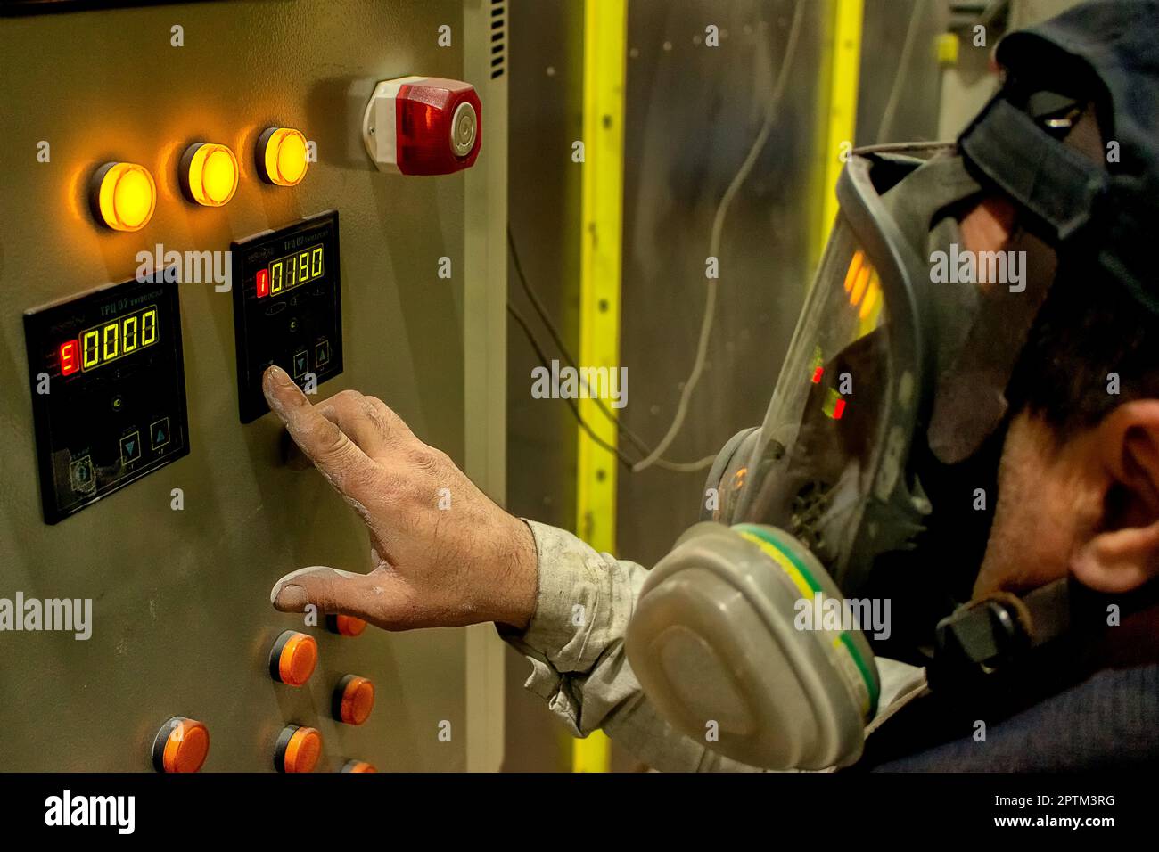 a white man in a work mask stands at the machine and presses the ...
