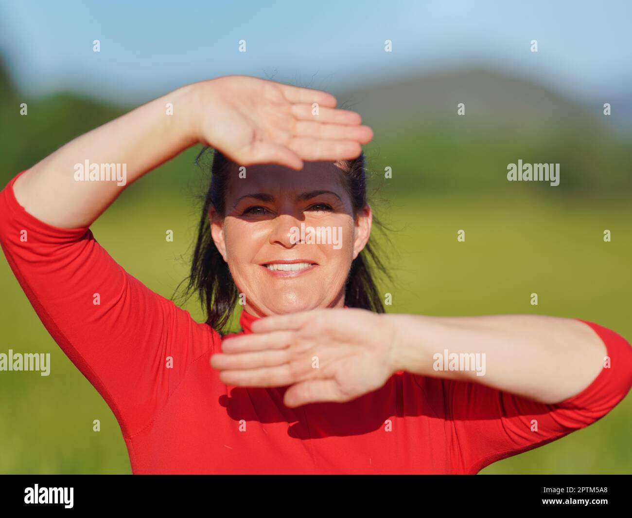 Woman in red dress standing in green field, shading her eyes from sun ...