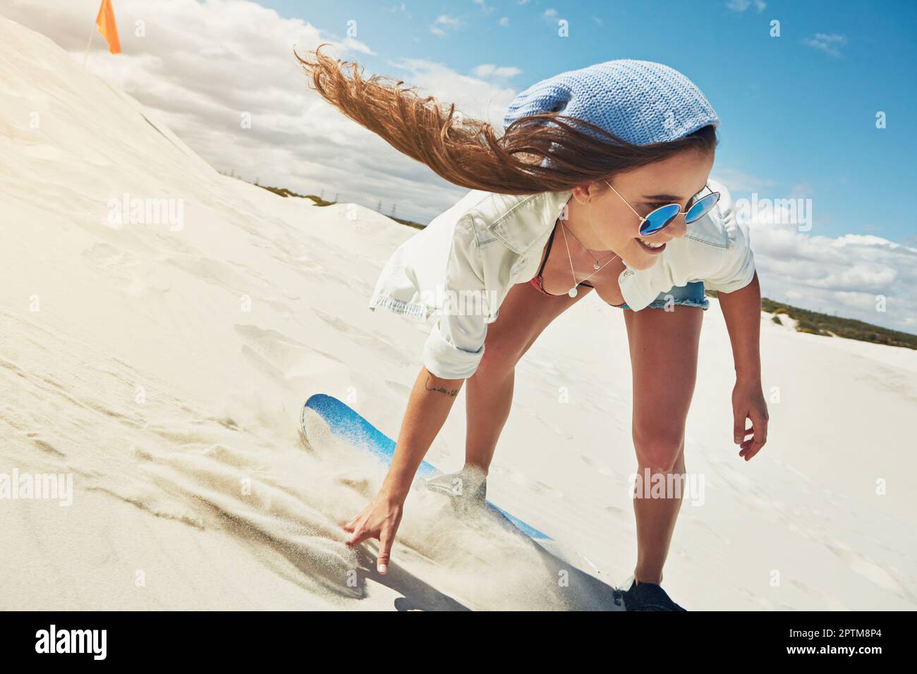 Speeding down the sand dunes. a young woman sand boarding in the desert ...