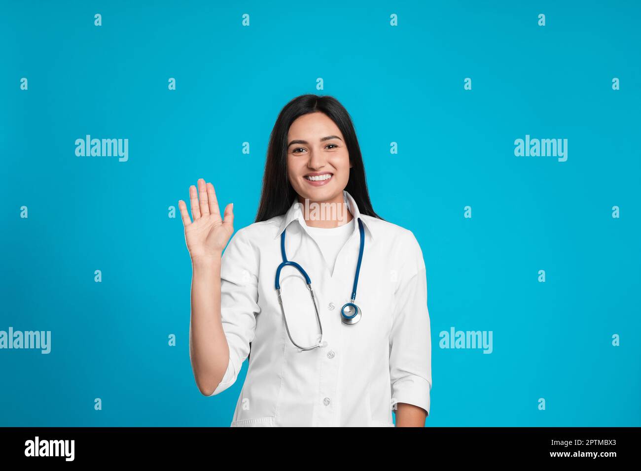 Happy female doctor waving to say hello on light blue background Stock ...